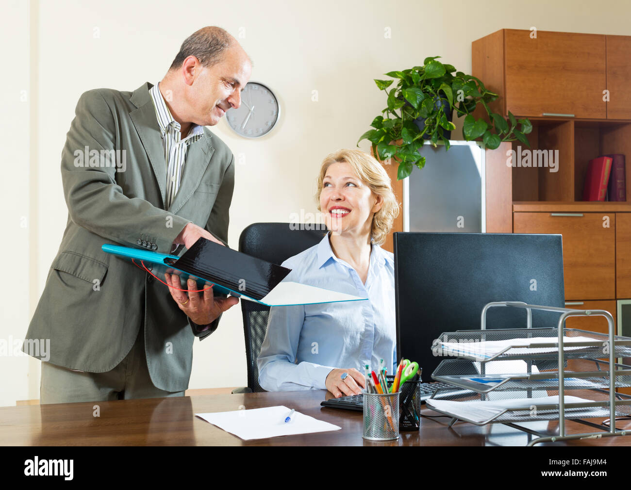 Elderly businessman with folder in hand, talking with his secretary ...