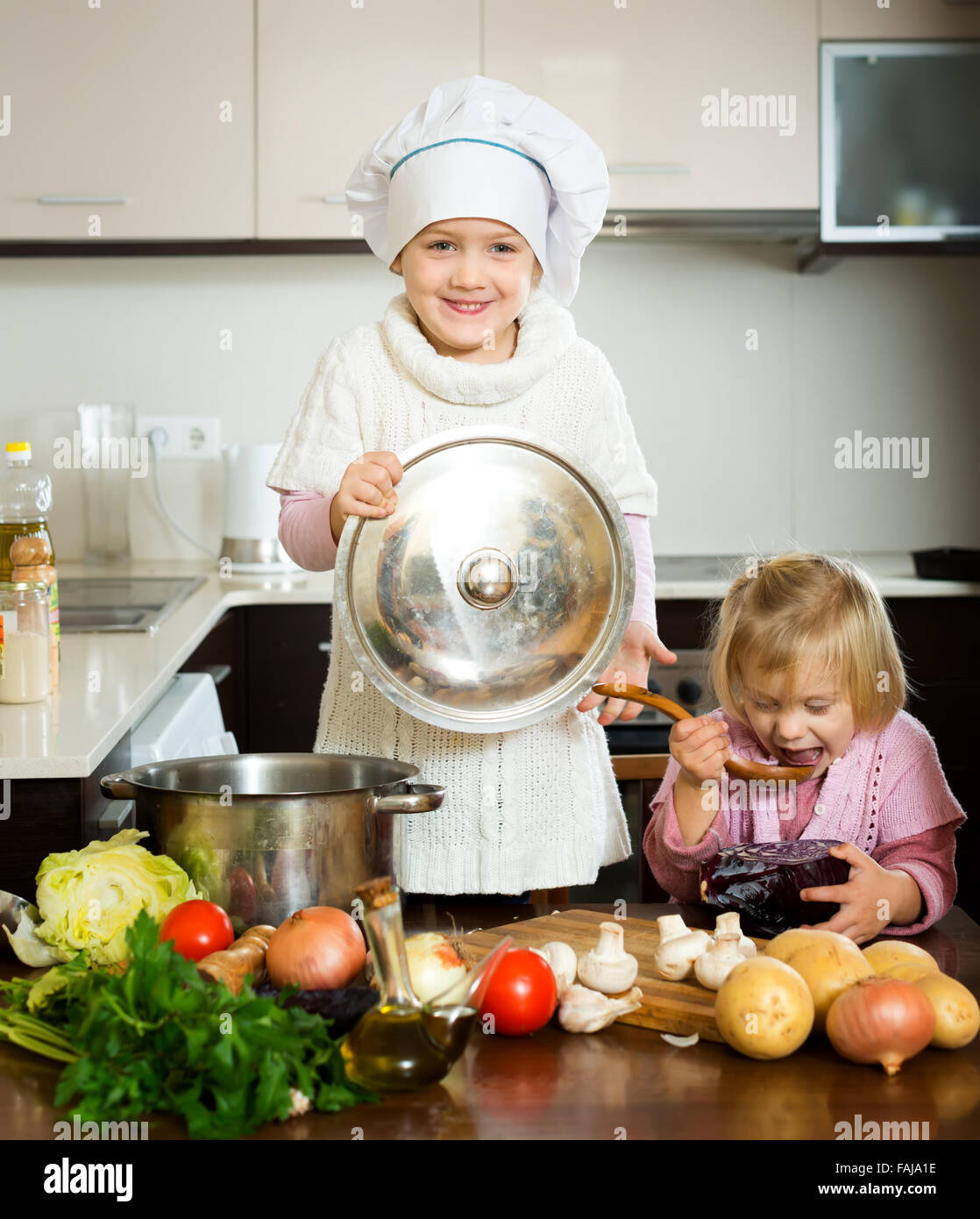 Little girls learning how to cook in the kitchen. One girl is holding a ...