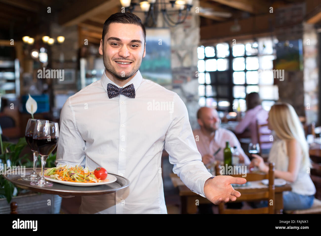 Happy smiling handsome waiter in a restaurant holding a tray with a ...