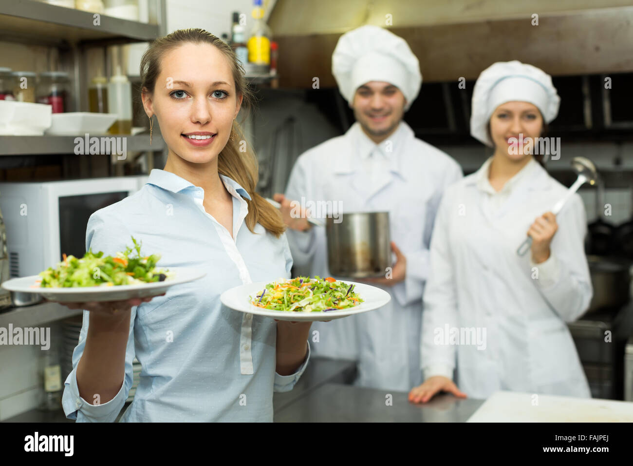 Two chefs and female waiter at restaurant kitchen. Selective focus ...