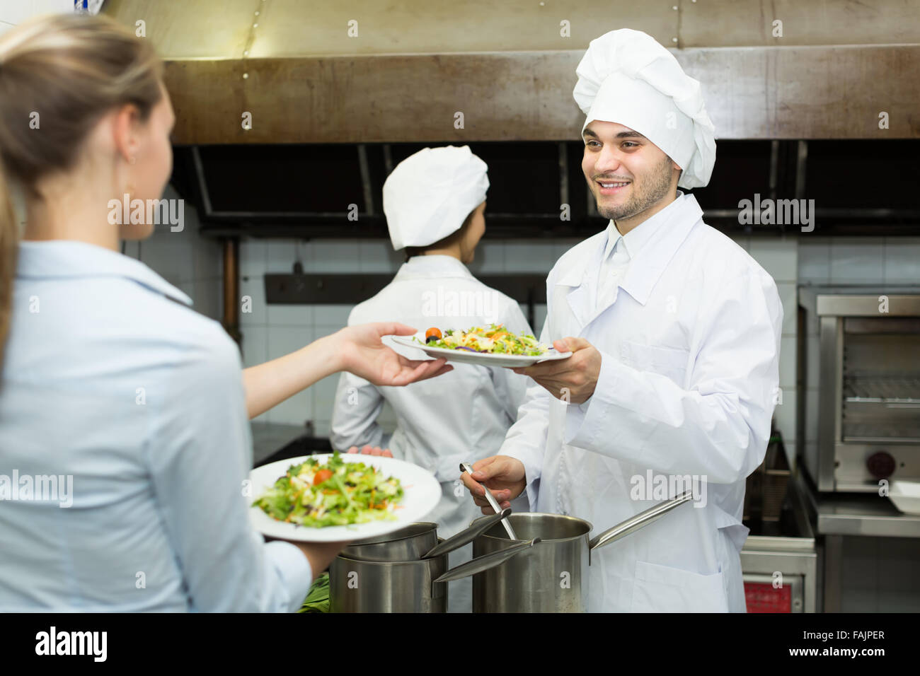 Smiling cook gives to young waitress plates with prepared meal at ...