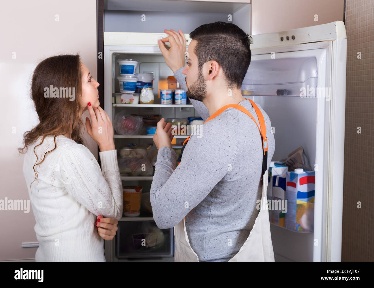 Housewife showing broken refrigerator to serious repairman Stock Photo ...