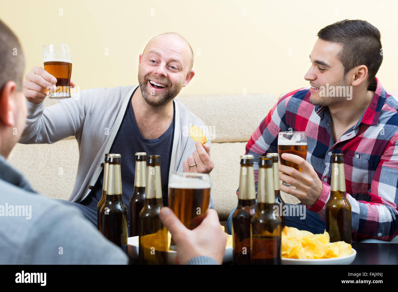 Three happy young guys drinking beer and talking at home Stock Photo - Alamy