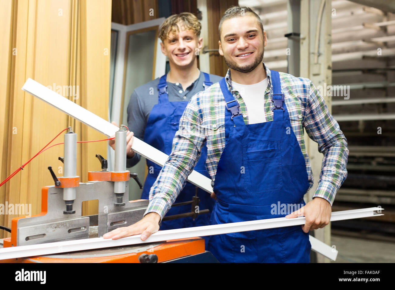 A couple of happy adult workers are working around the milling machine ...
