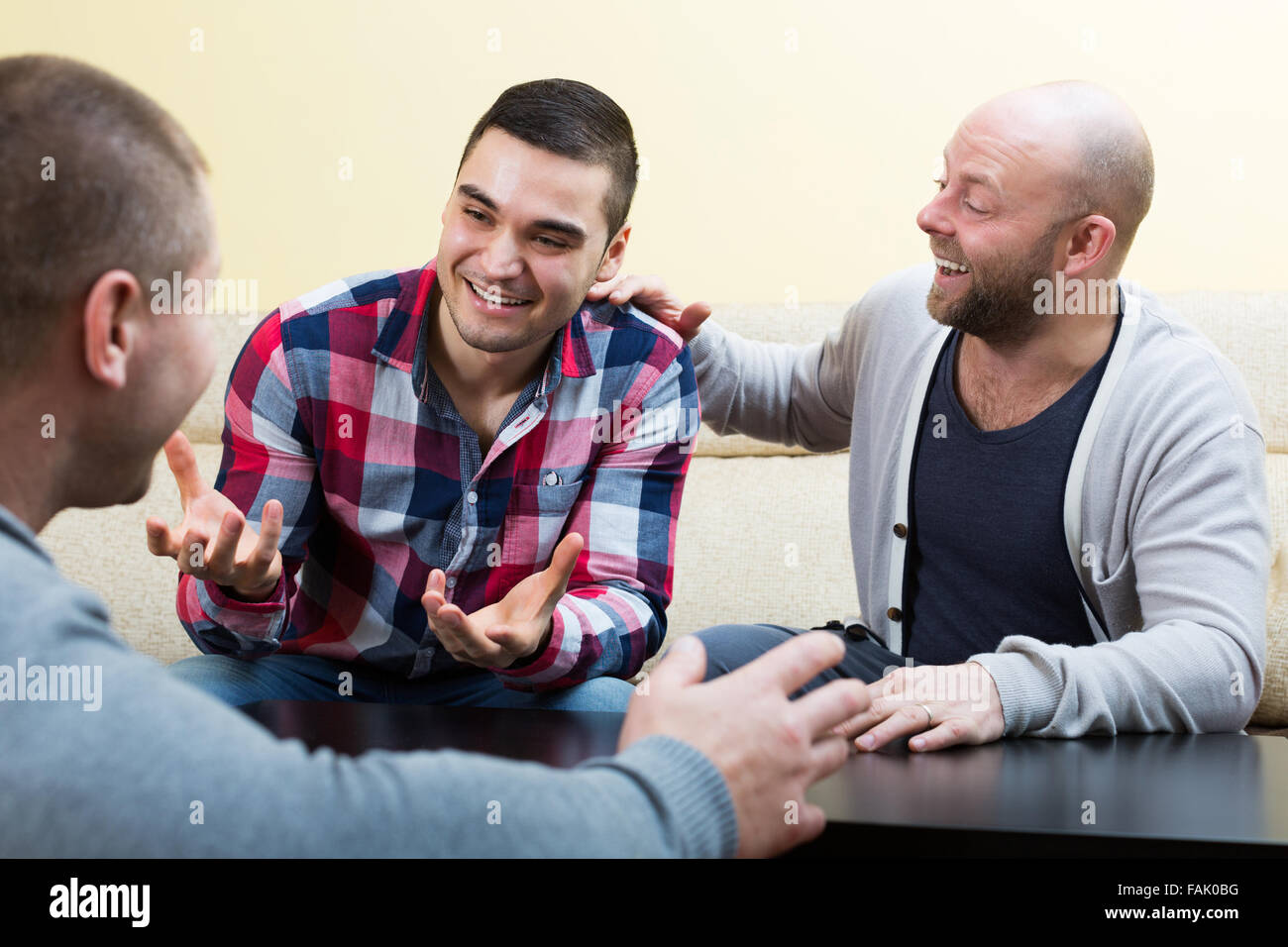 Three adult men talking and laughing at living room Stock Photo - Alamy