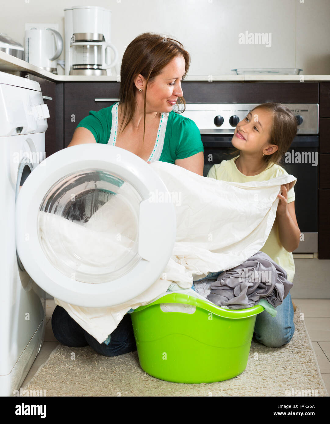 Home family laundry. Smiling mother with little daughter loading ...