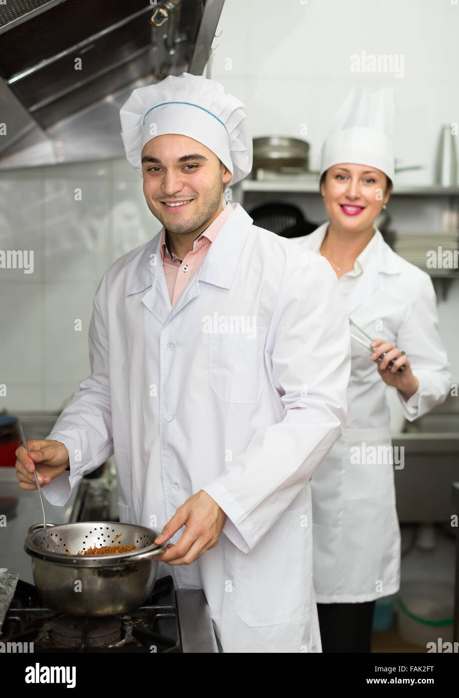 Two smiling professional cooks working together at restaurant kitchen ...
