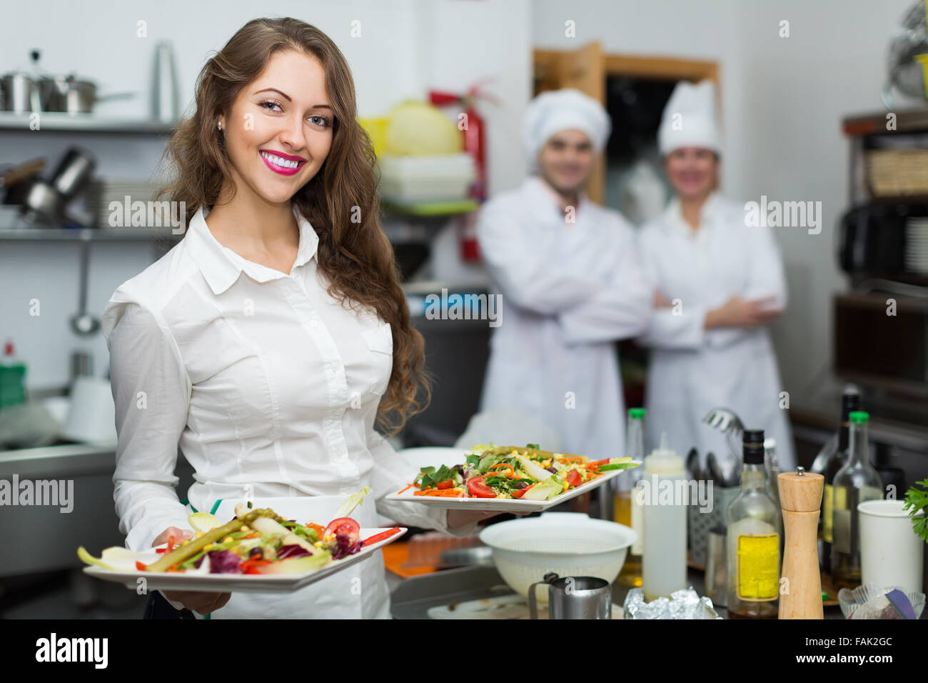 Smiling young waitress take dishes with food at kitchen Stock Photo - Alamy