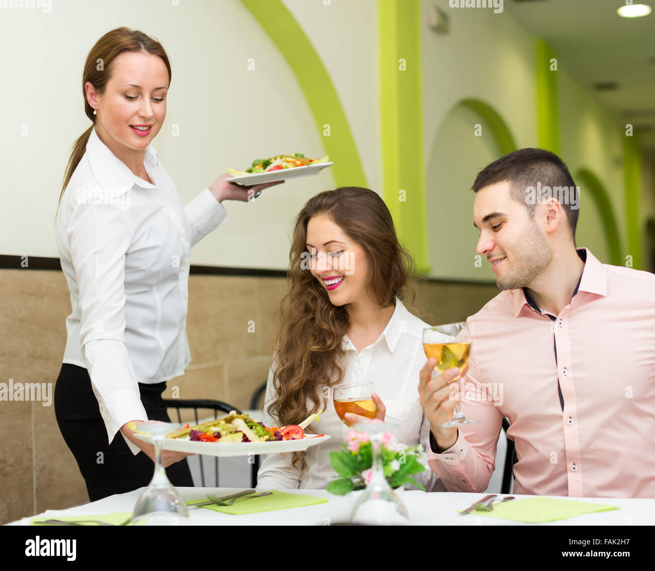 Female waiter with plates in hands serving guests table in restaurant ...