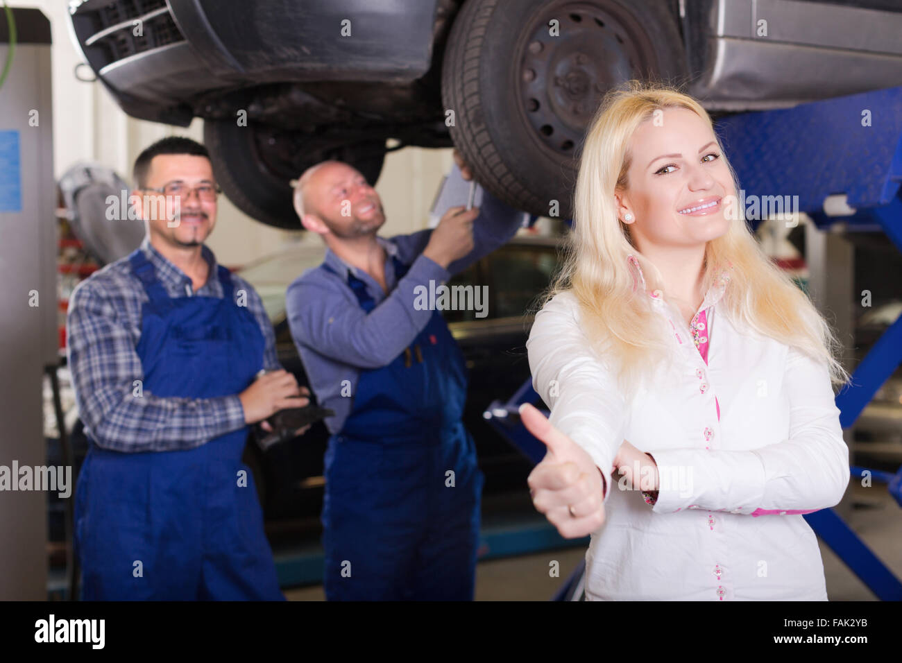 Service crew and happy driver standing near car and smiling indoor ...