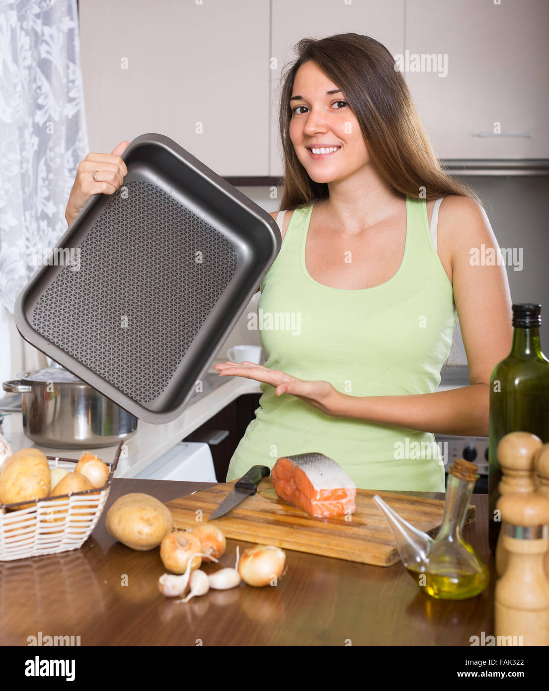 Positive young woman cooking salmon fish in frying pan at kitchen Stock ...