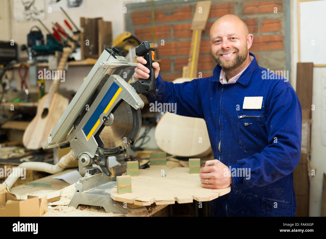 Smiling adult professional woodworker on lathe at musical instrument ...