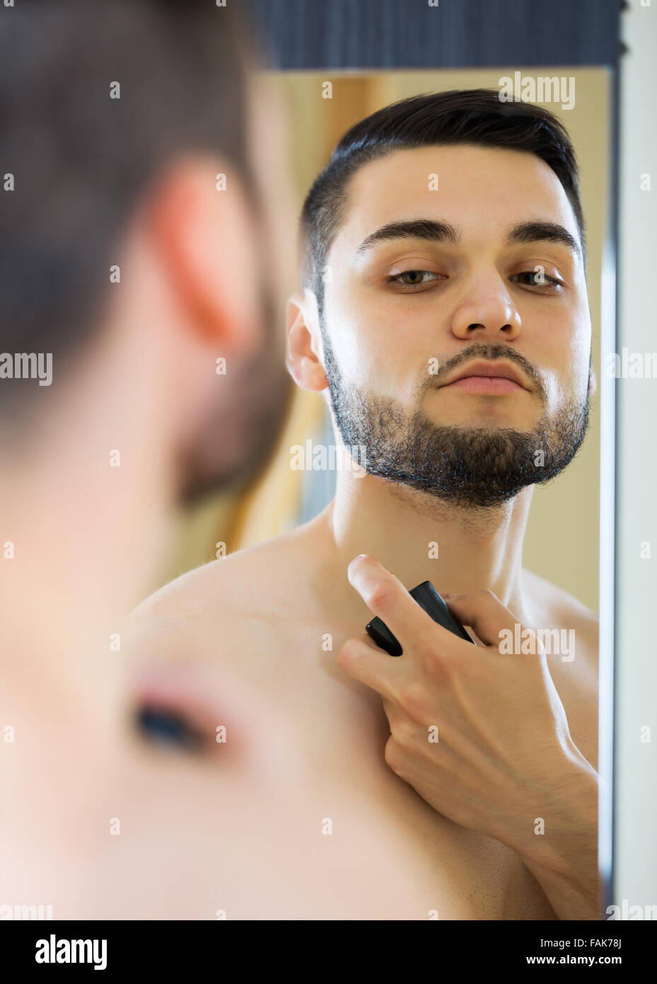 Serious young man spraying fragrance perfume at home Stock Photo - Alamy