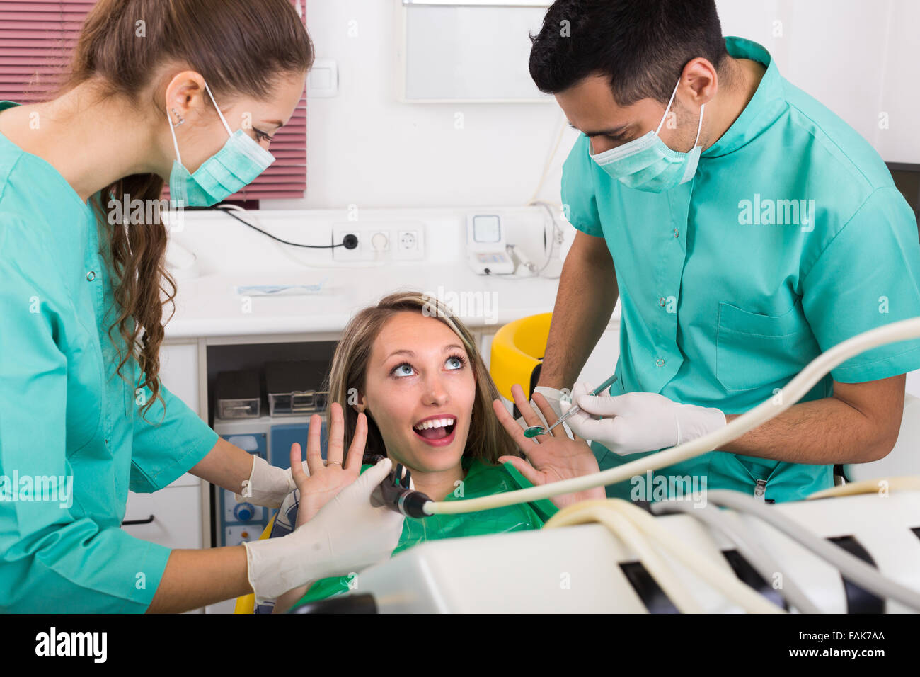 Male dentist with assistant and scared female patient at surgery office ...