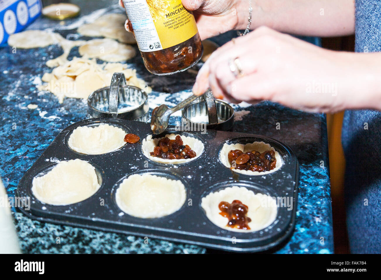 Making mince pies adding mincemeat to pastry cases cooking in kitchen ...