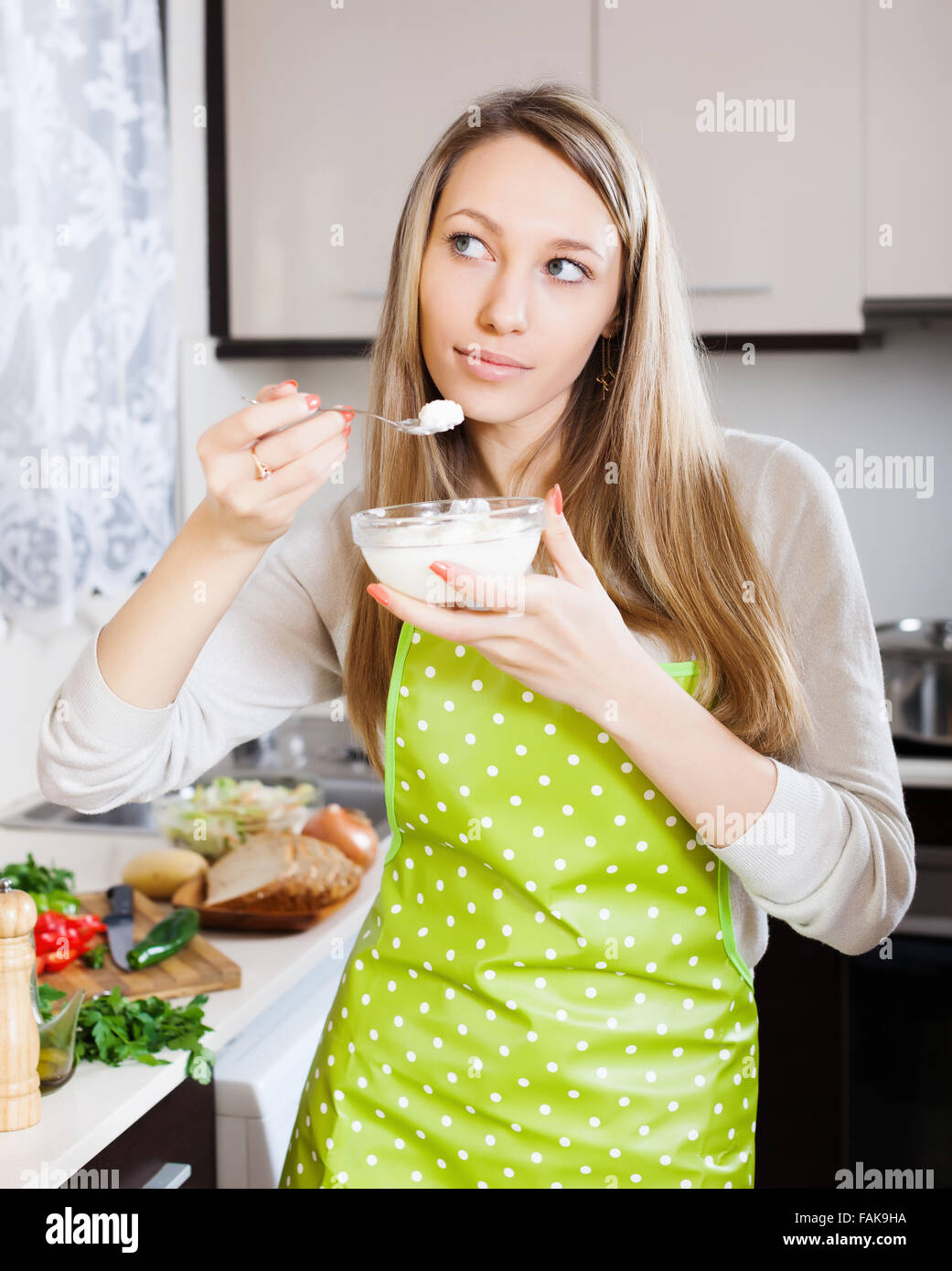 Smiling woman in apron eating curd cheese in kitchen Stock Photo - Alamy