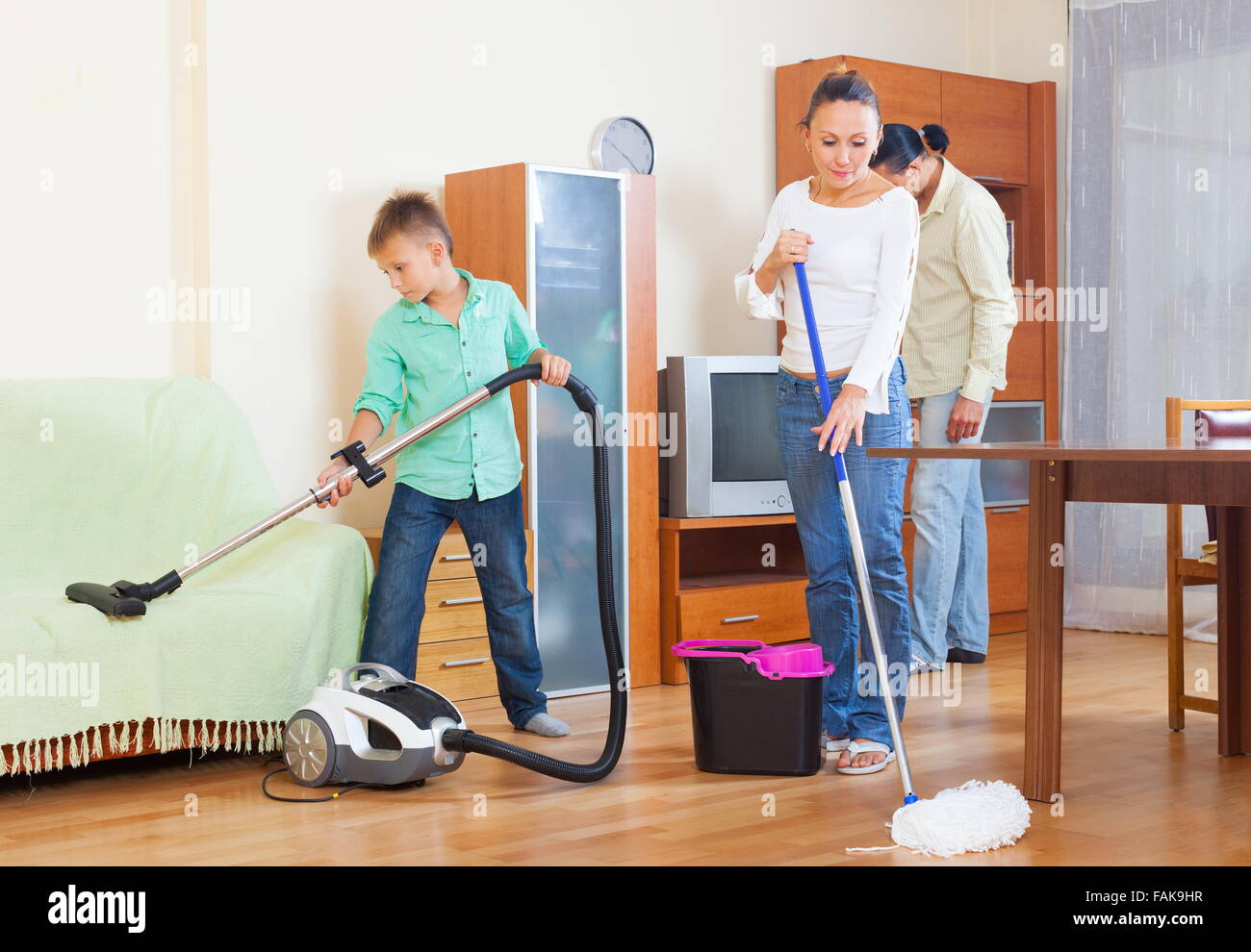 Ordinary family of three with teenager doing housework together in home ...