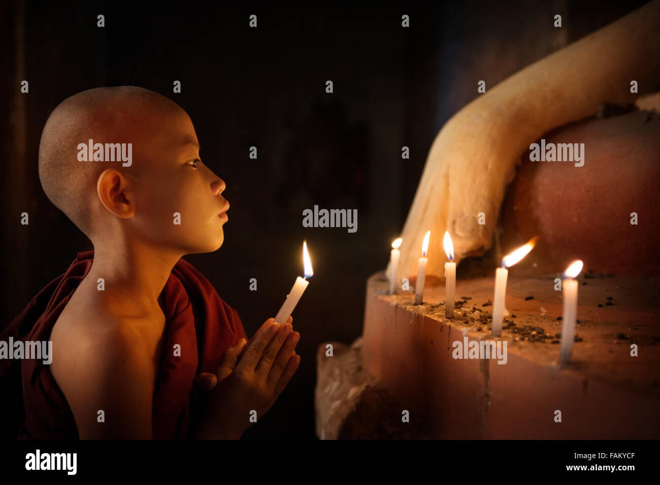 Portrait of young novice monk praying with candlelight inside a ...