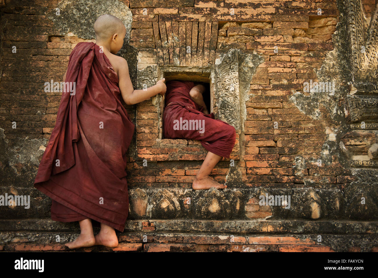 Two playful young novice monks climbing into Buddhist temple from ...