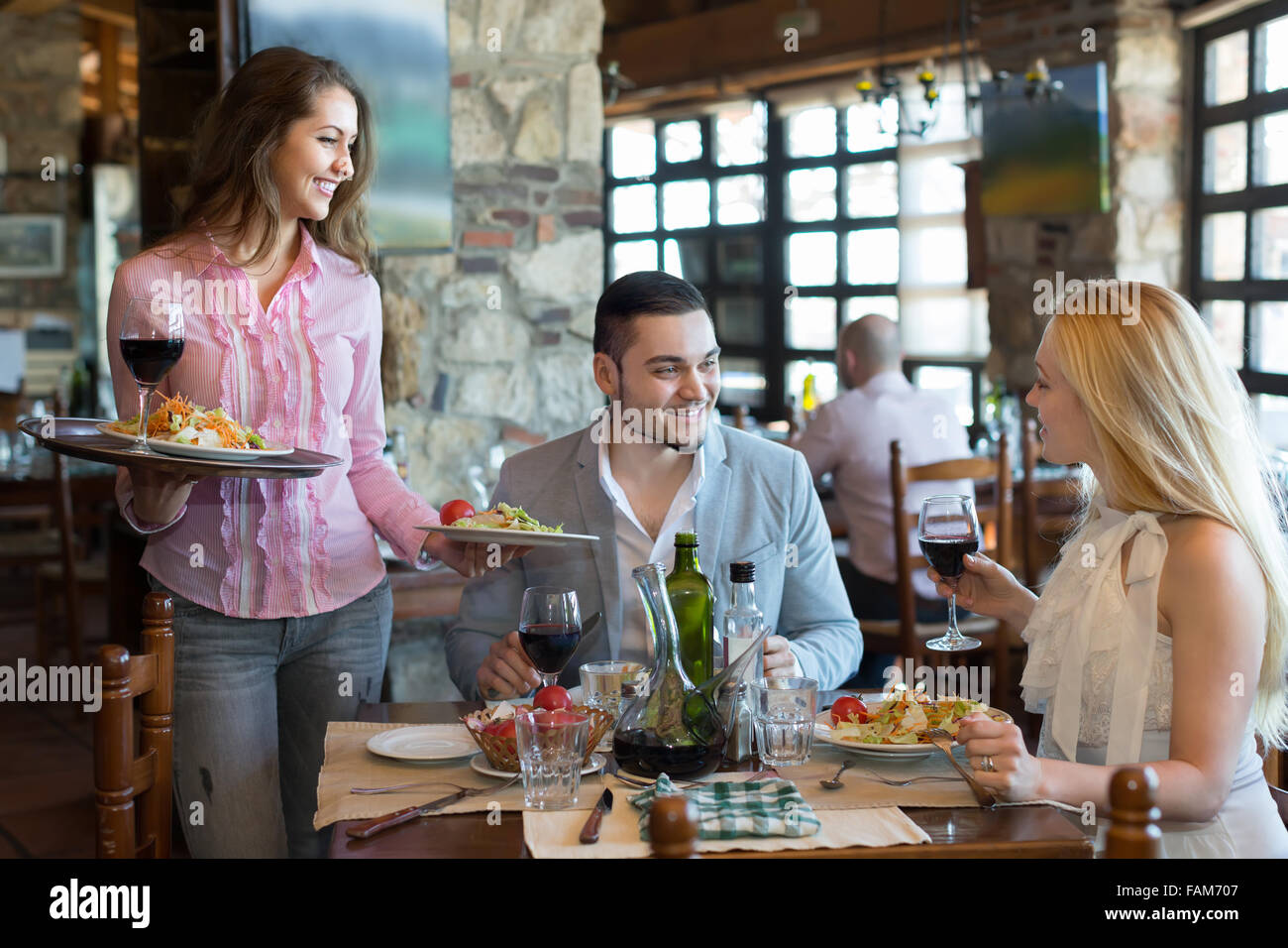 Smiling young brunette female waiter serving restaurant guests ...