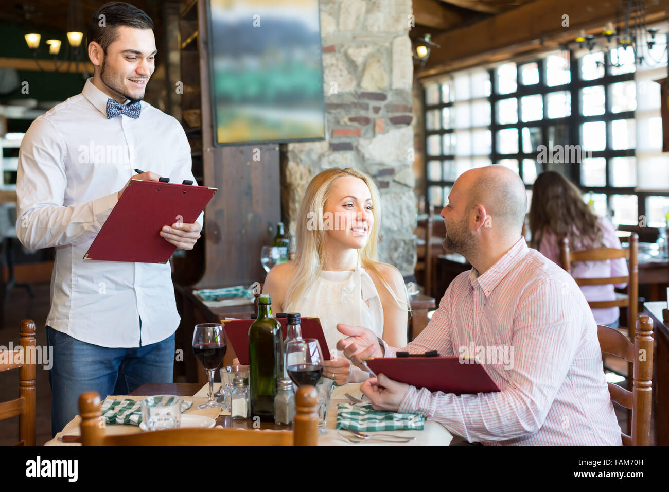 Cheerful young male waiter serving restaurant guests at table ...