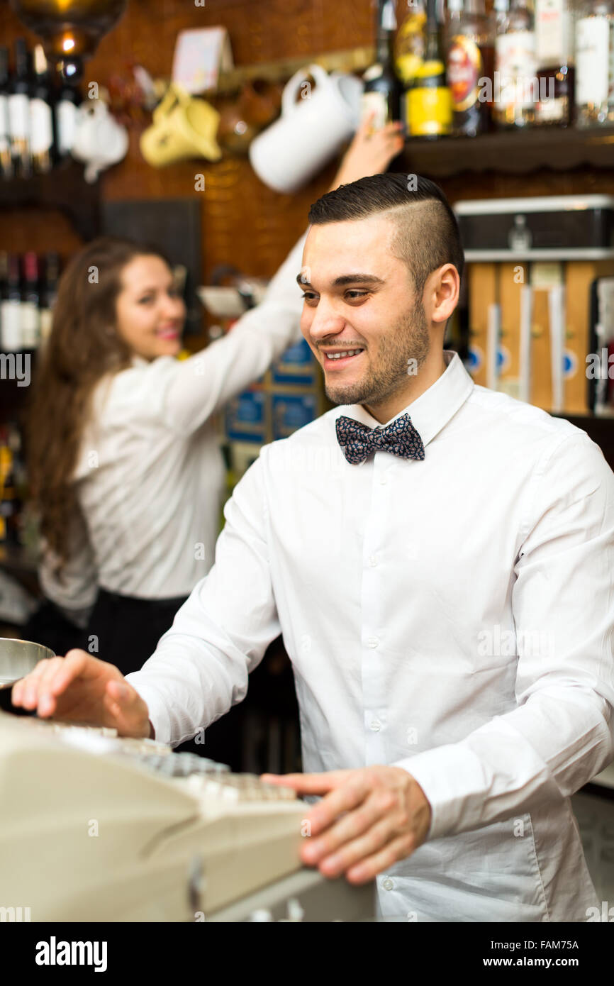 Handsome male cashier working in a bar while his female colleague is ...