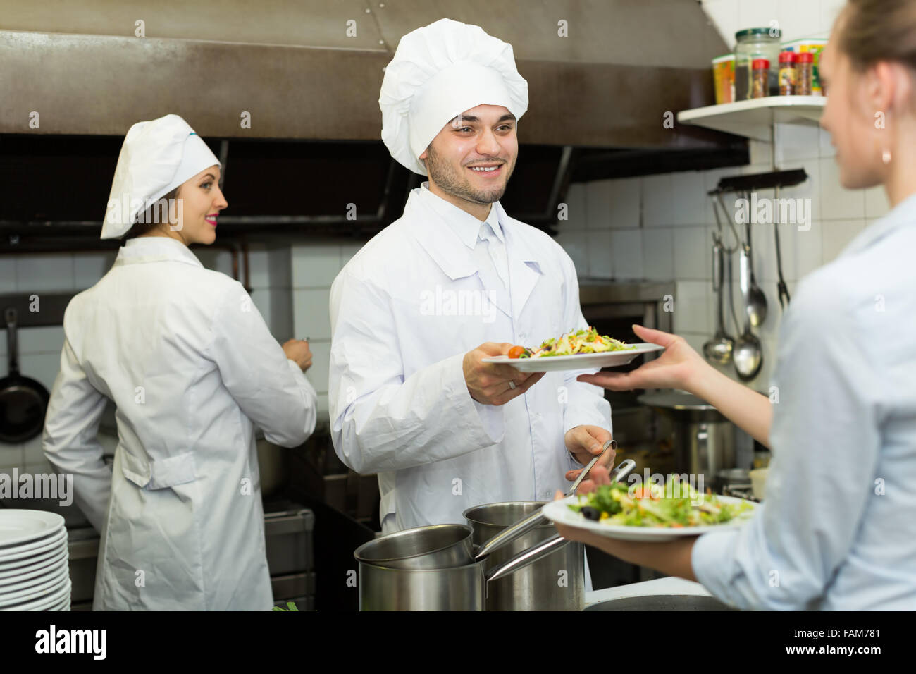 Team of positive chefs and young waiter at restaurant kitchen Stock ...