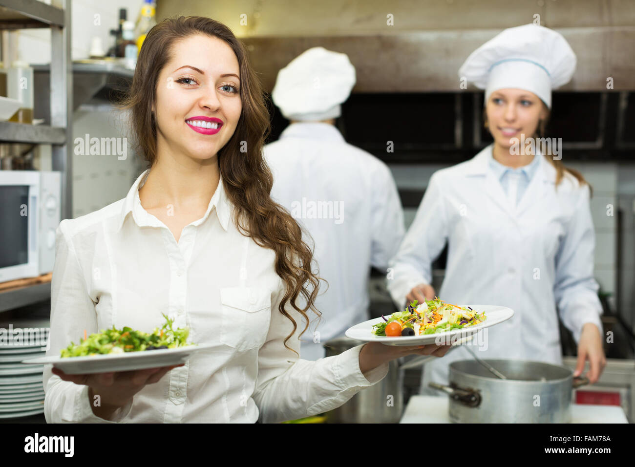Cook gives to woman waitress plates with prepared meal at restaurant ...