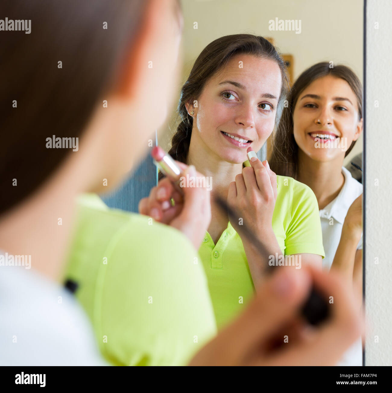 Smiling teenage girlfriends having fun while putting make up in front ...