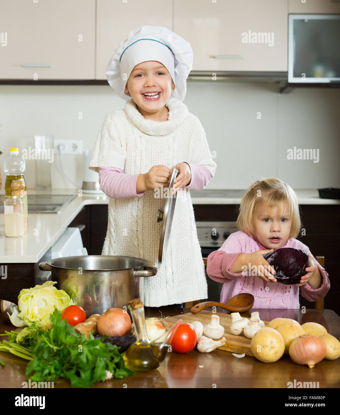 Happy little girls help each other to cook soup for dinner on kitchen ...