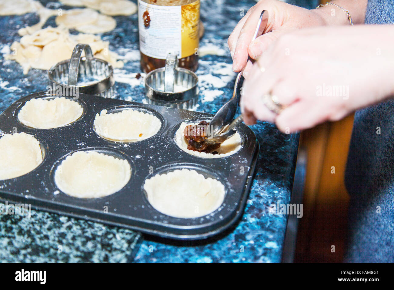 Making mince pies adding mincemeat to pastry cases cooking in kitchen ...