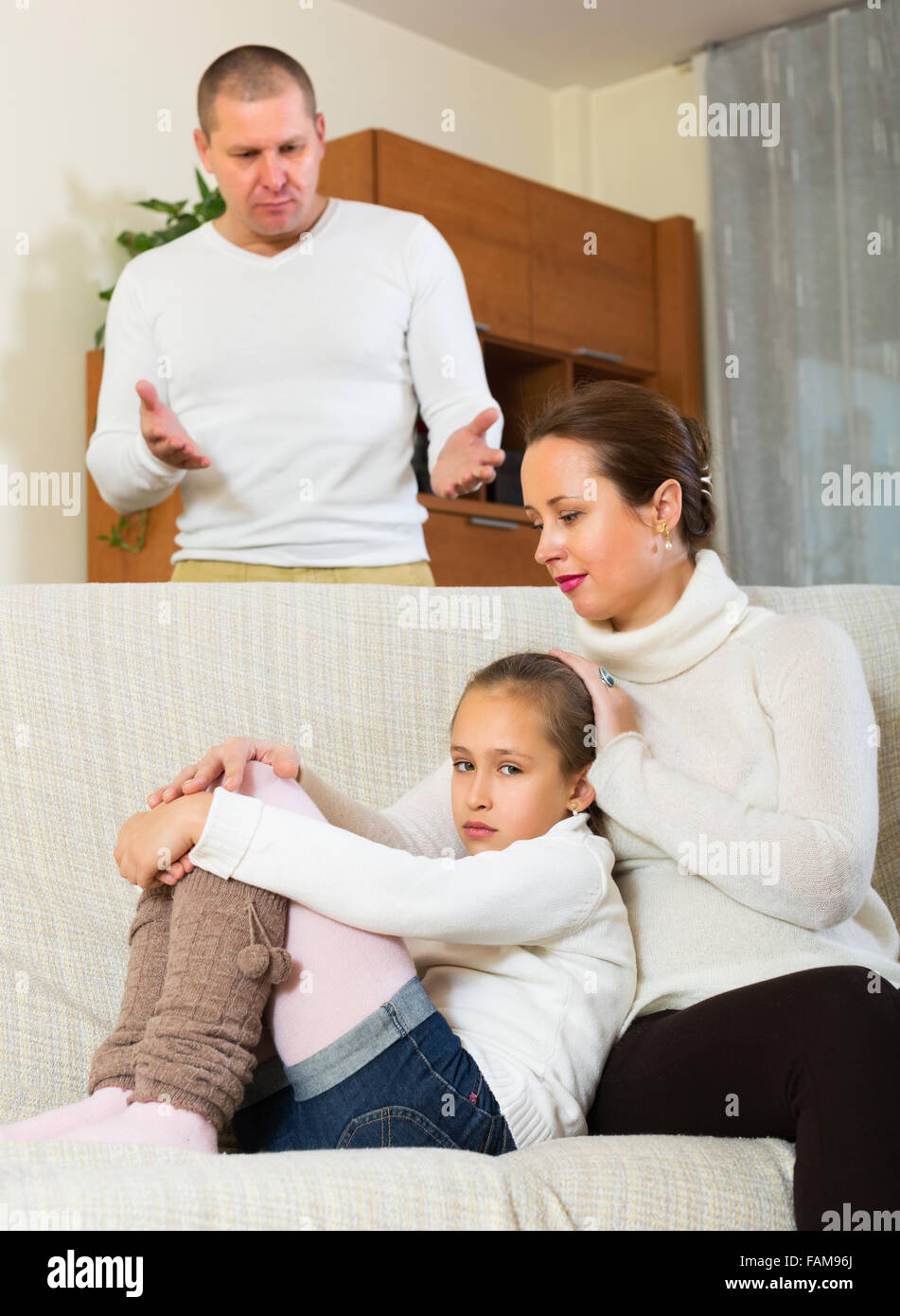 Sad mother comforting litlle daughter in livingroom and angry father ...