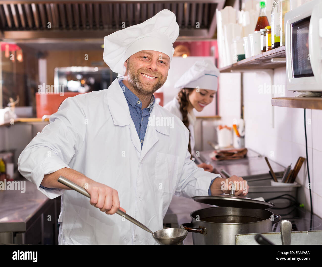 Portrait of hospitable smiling chef and his helper at fastfood place ...