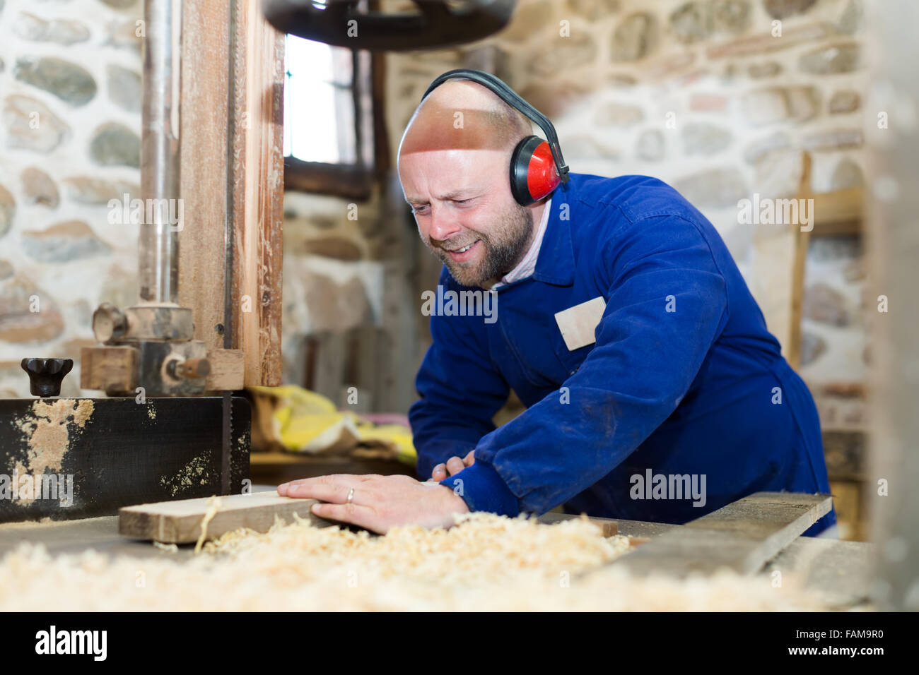 Professional male woodworker in a blue uniform is cutting plank of wood ...