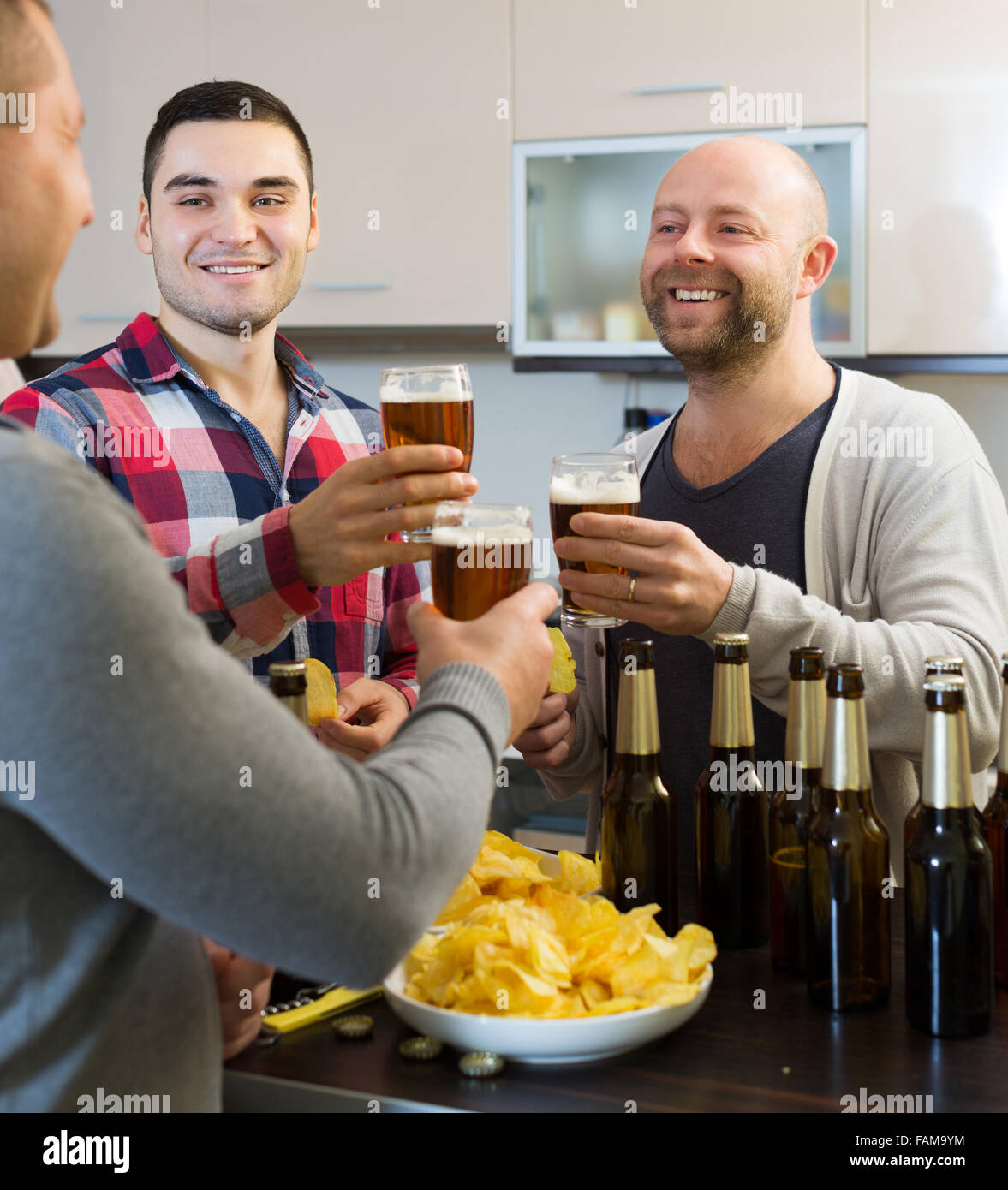 Three adult men drinking beer and laughing at house party Stock Photo ...