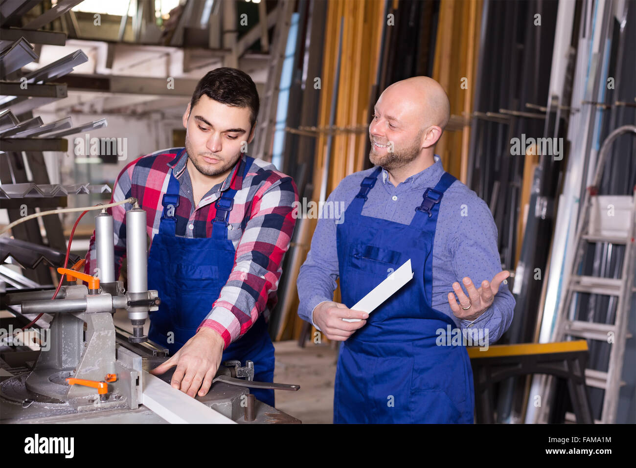 Two happy workmen in uniform working on a machine in PVC shop Stock ...