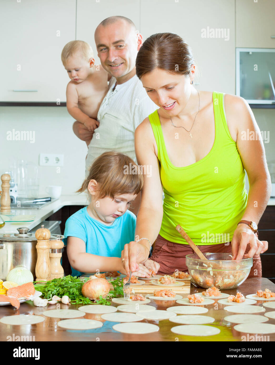 Happy family of four making dumplings with fresh fish with stuffing and ...