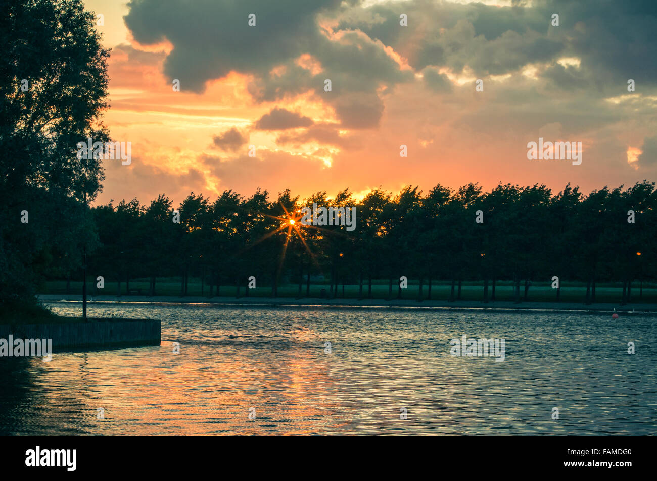 The sun setting behind trees on a lakeside Stock Photo - Alamy