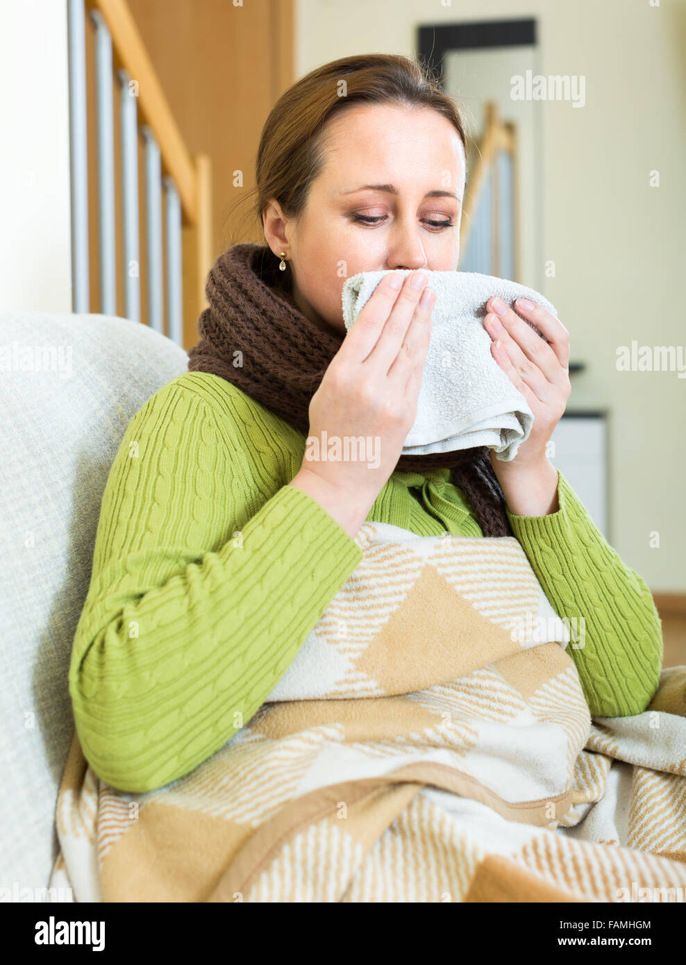 Sick adult beautiful woman on a couch at home. She is sitting under a ...