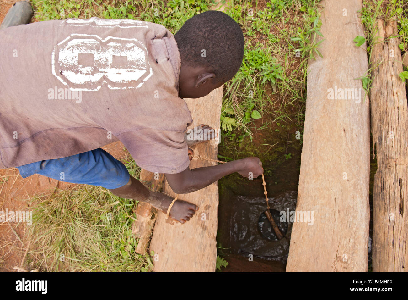 Child drawing water up from a deep well with bucket and rope. Kenya ...