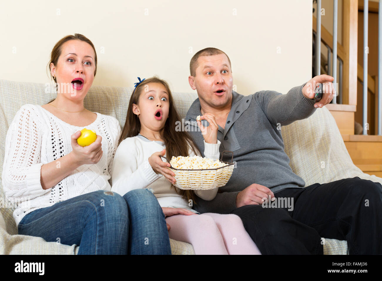 Parents and daughter watching TV show together at home. Focus on woman ...