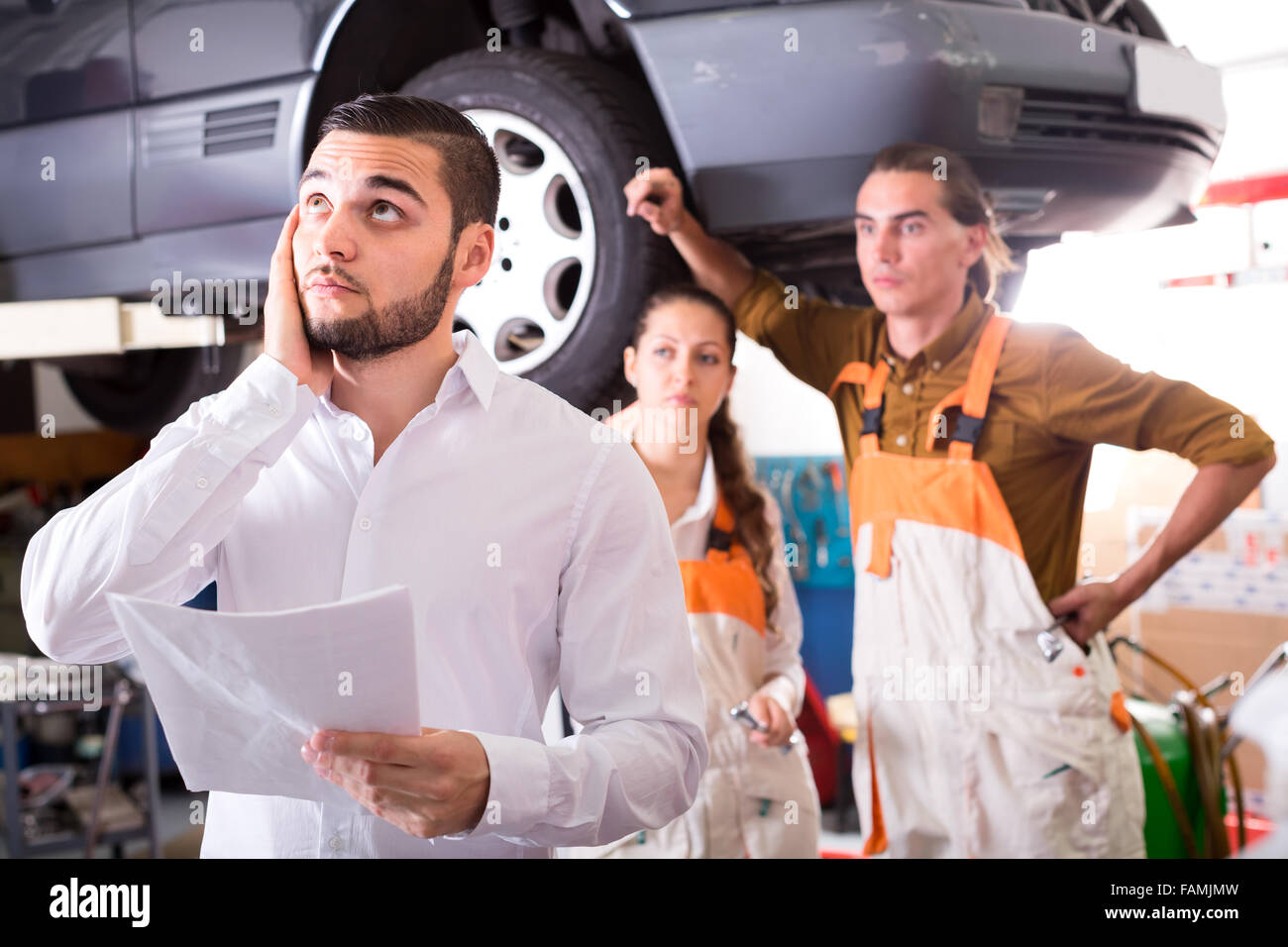 Worried client standing in a car shop holding his cheek with a repair ...