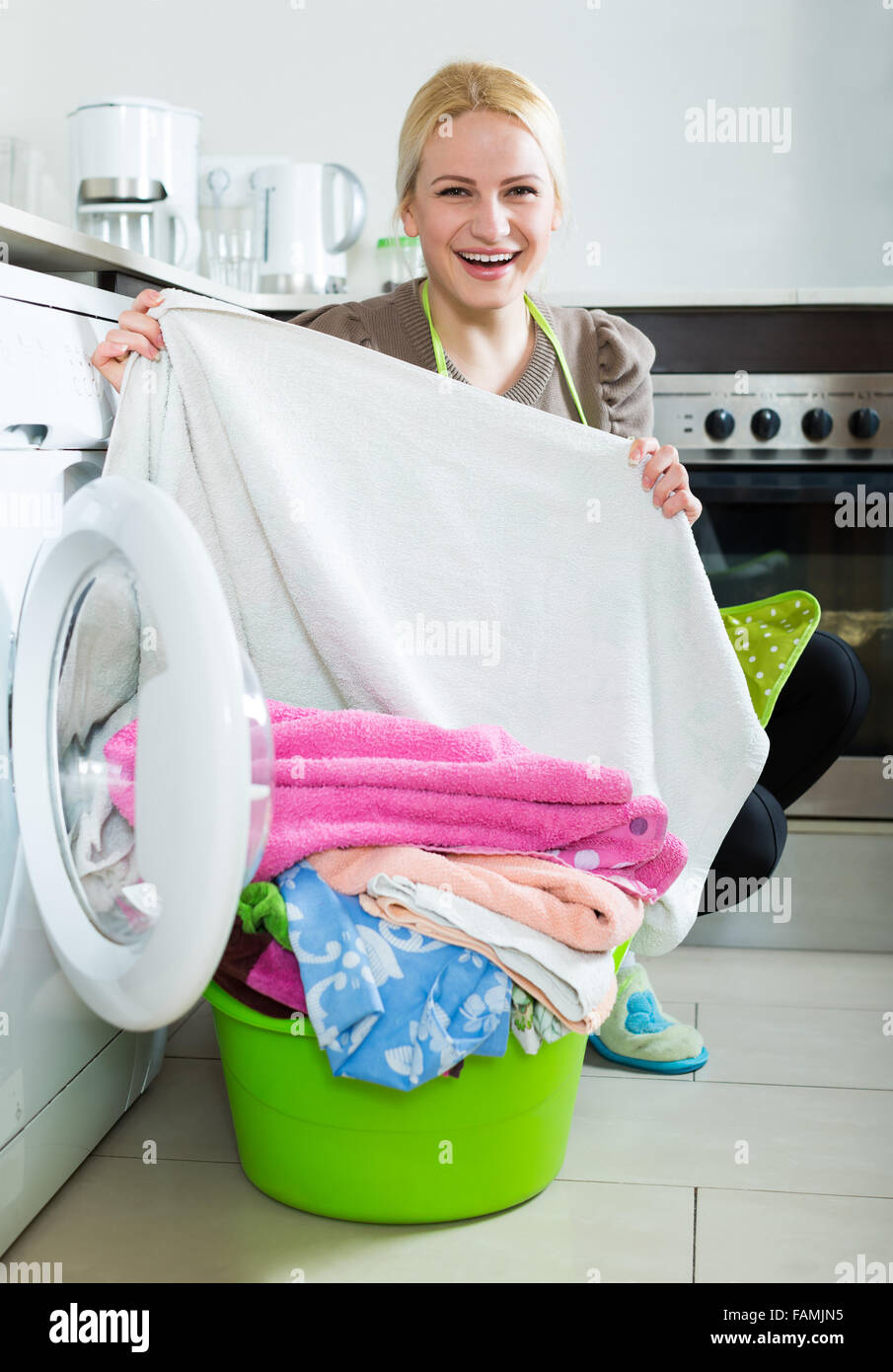 Home laundry. Happy blonde woman loading clothes into washing machine ...