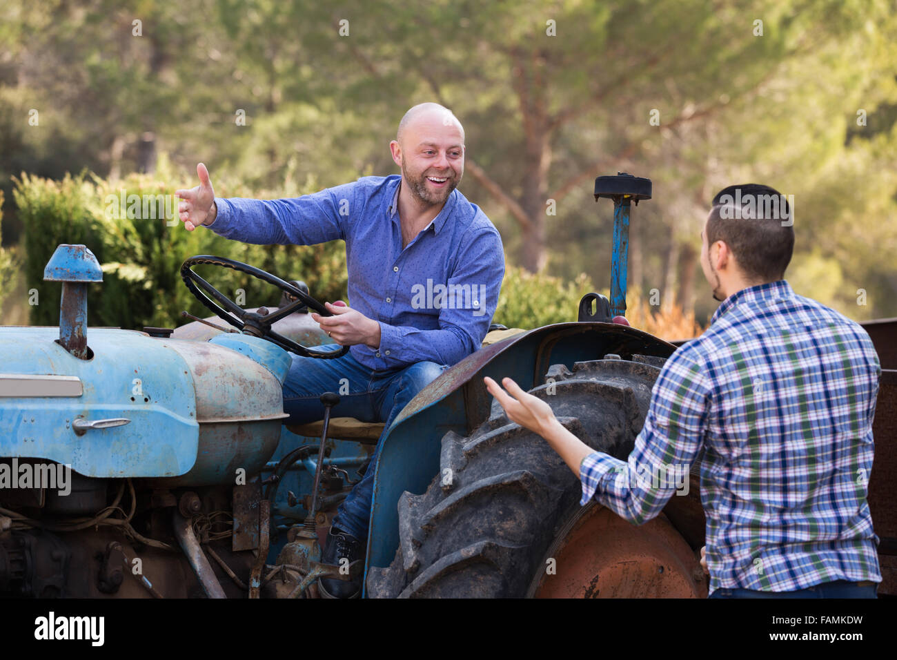 Two positive male drivers working with tractor and chatting outdoor ...