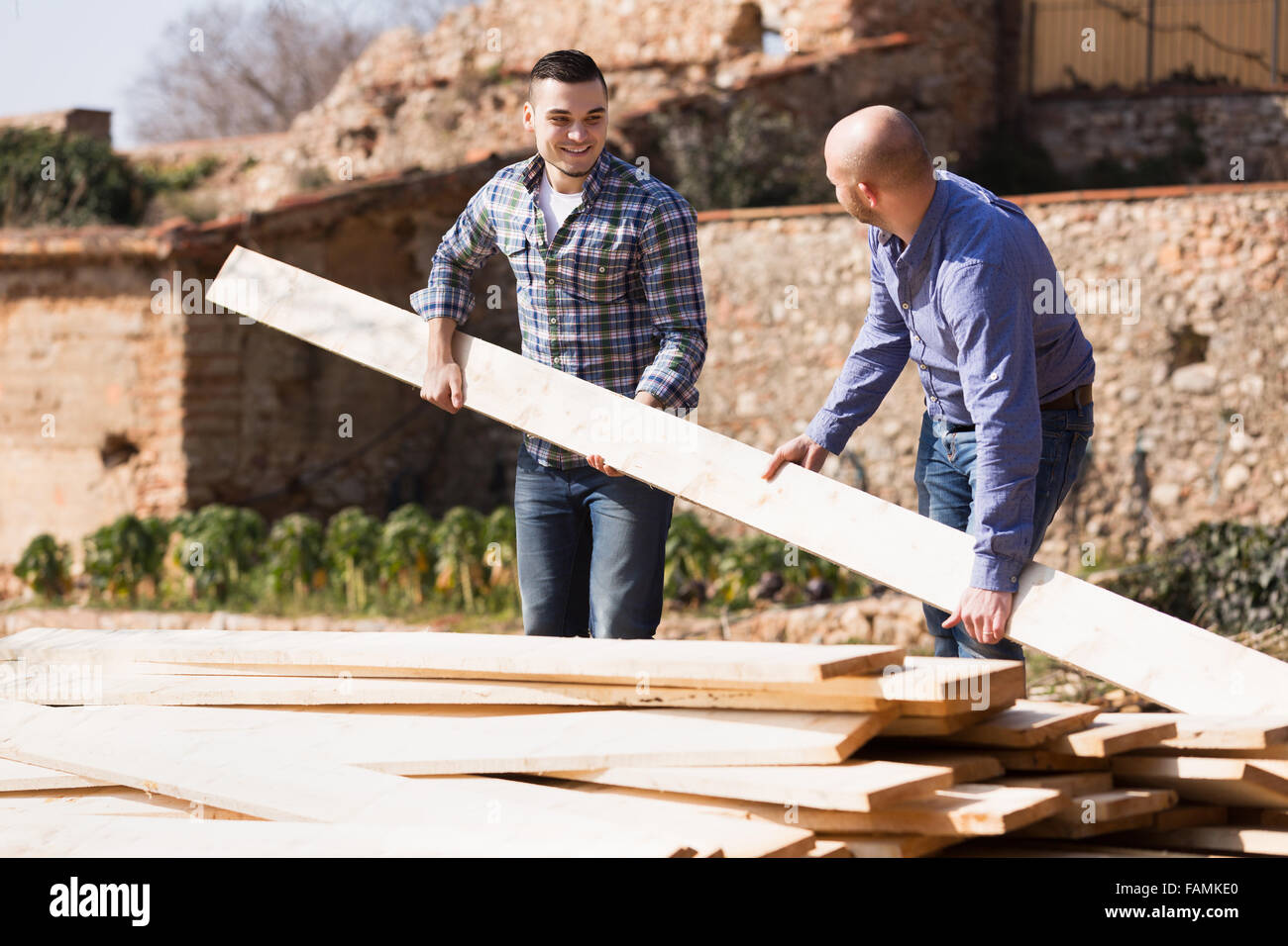 Two adult positive male builders carrying over plane boards at site ...