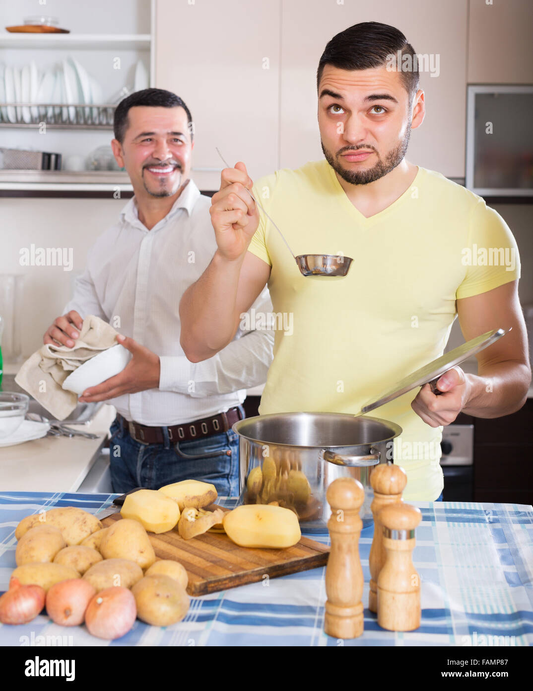 Adult son helping smiling father to prepare vegetable stew at kitchen ...