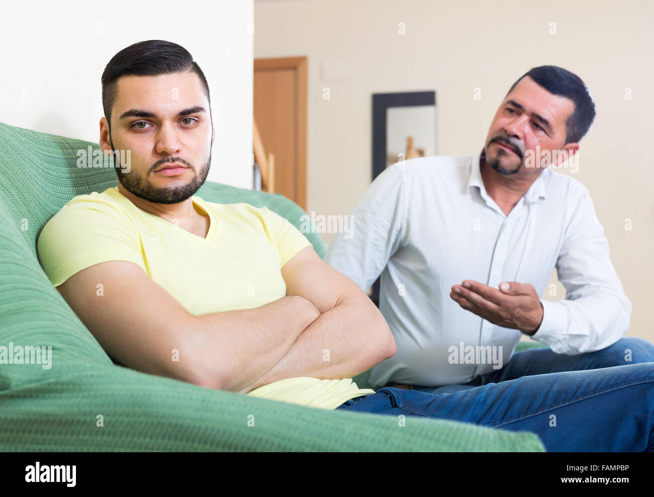 Portrait of two male adults sitting on couch and being at odds at home ...