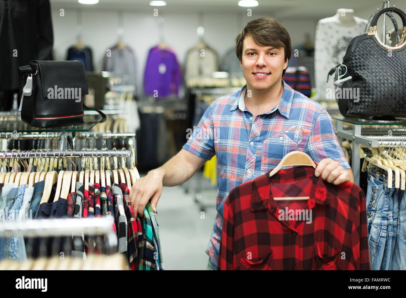 Young smiling guy choosing shirt at the clothing store Stock Photo - Alamy