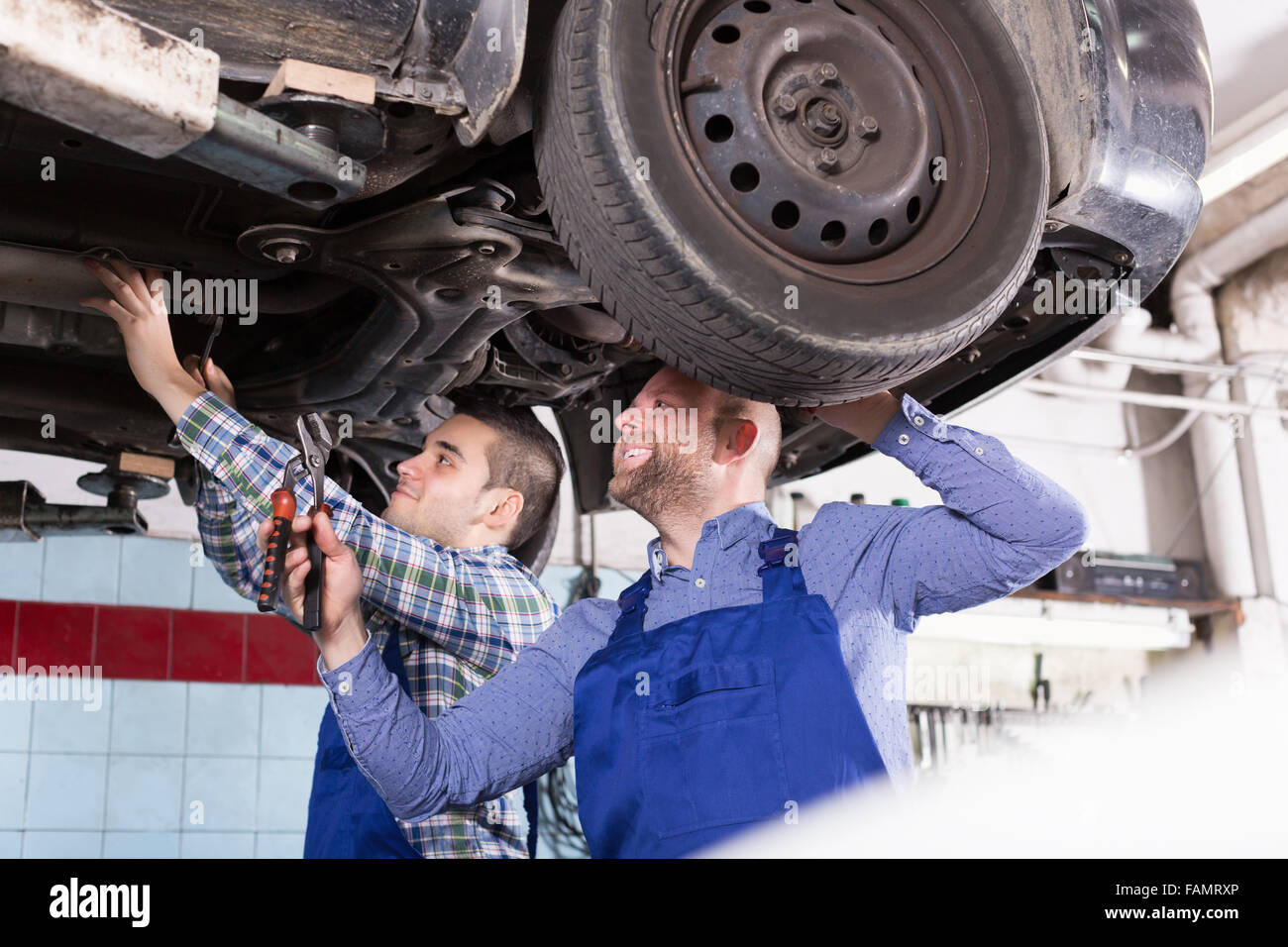Positive smiling adult mechanics repairing car of client Stock Photo ...