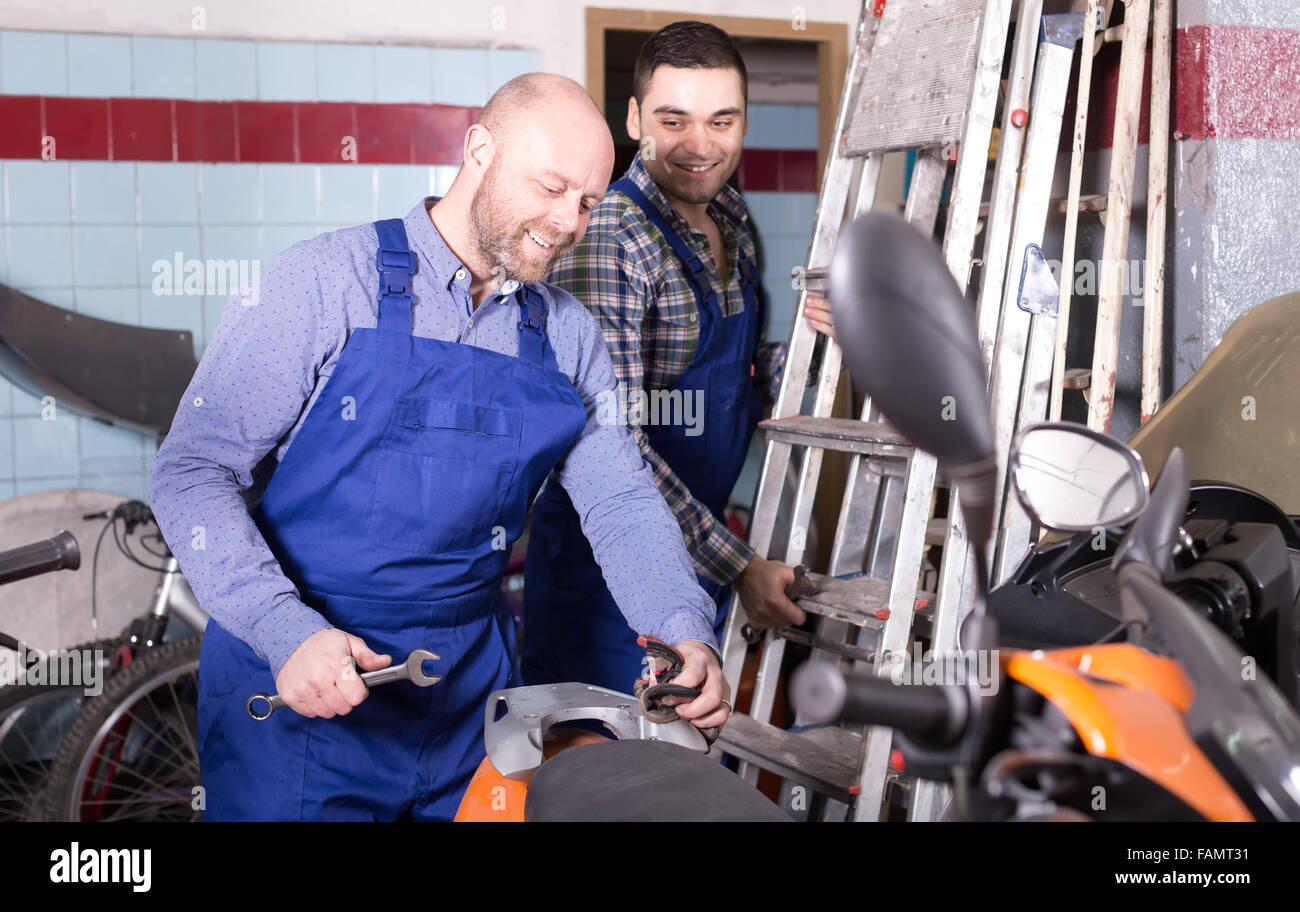 Professional mechanics doing moped and motorcycle service at station ...
